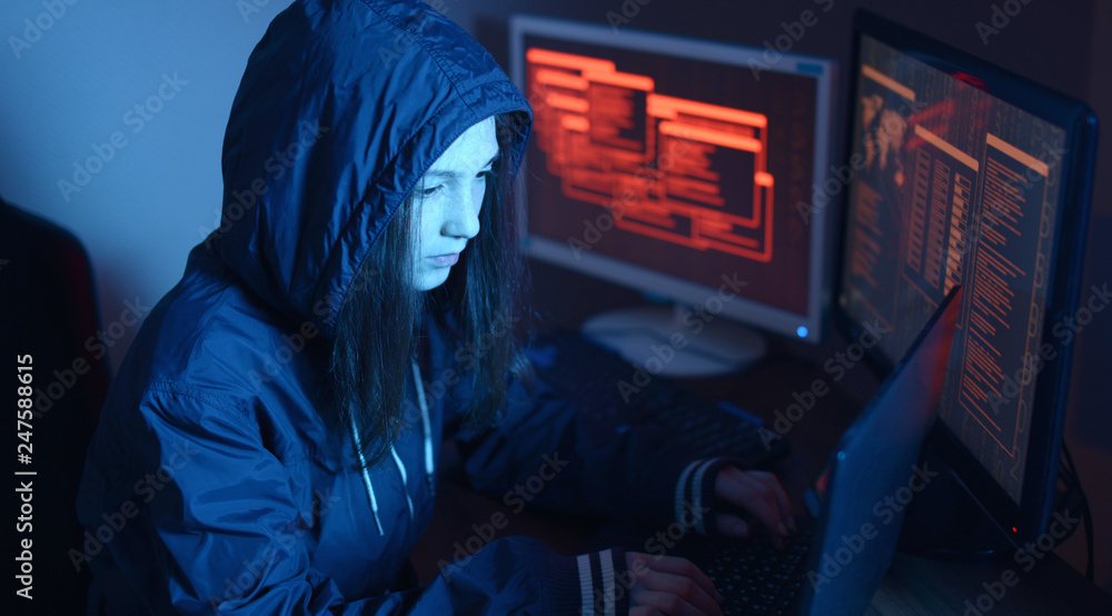 Girl hacker in a hood typing program code while committing a cybercrime hacking a firewall on ...