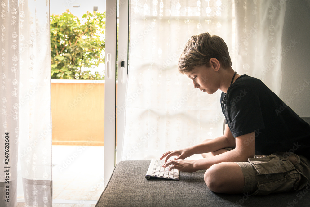 Beautiful blond child sitting on the couch at home using computer ...