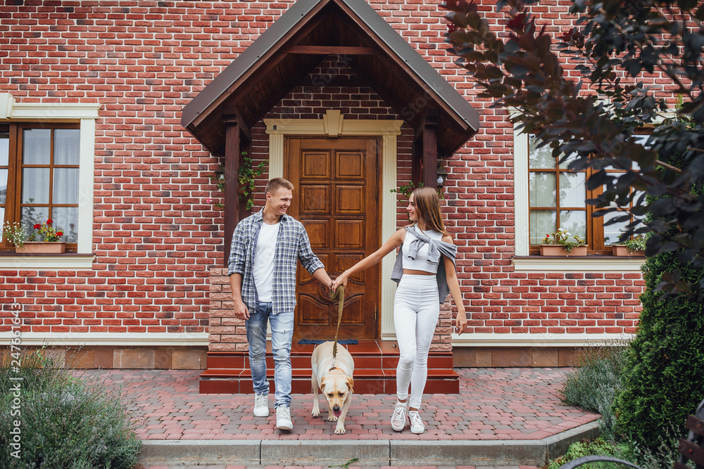 Portrait of excited couple standing outside new home with dog. Happy smiling family with ...