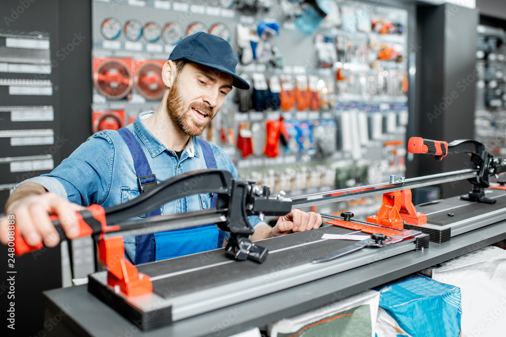 Handsome workman in uniform choosing professional tile cutter in the ...