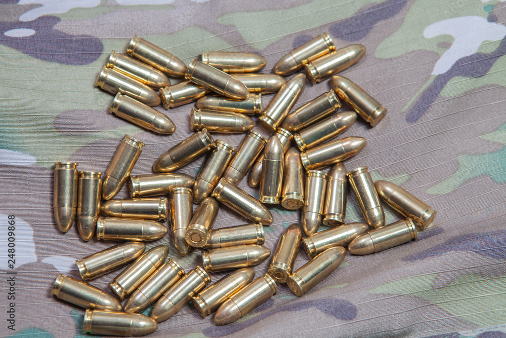 Golden 9mm pistol cartridges on camouflage background. Sport sgooting ...