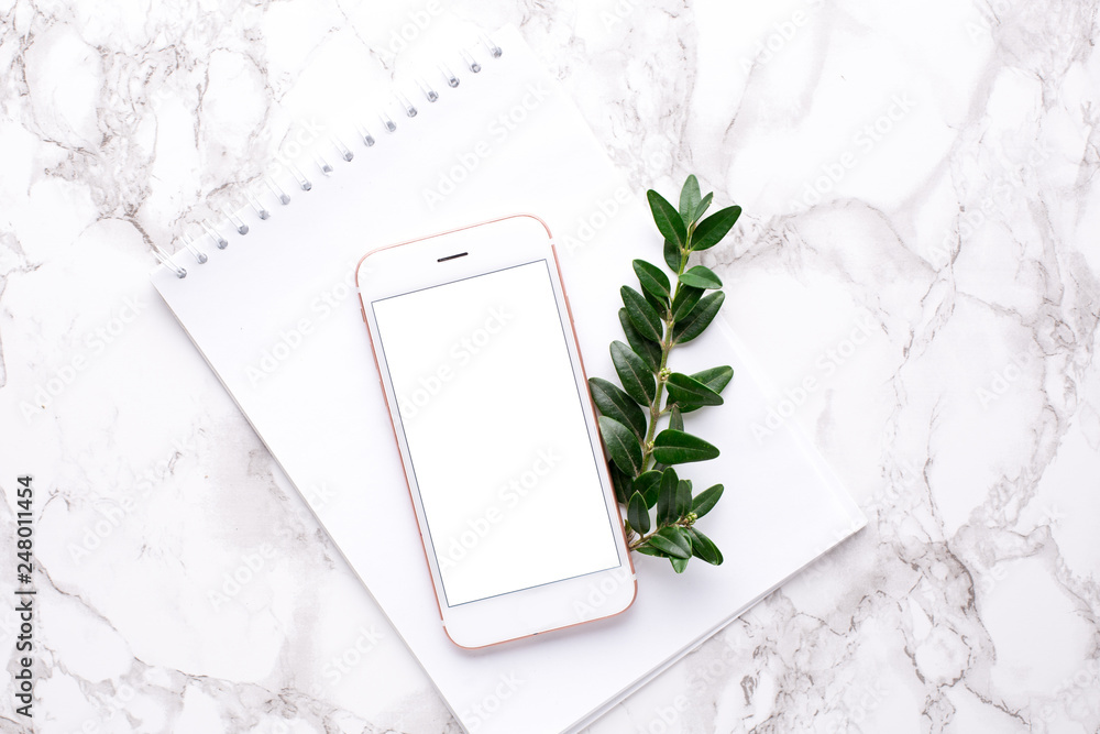 Mobile phone and white notebook on a marble background with greens ...