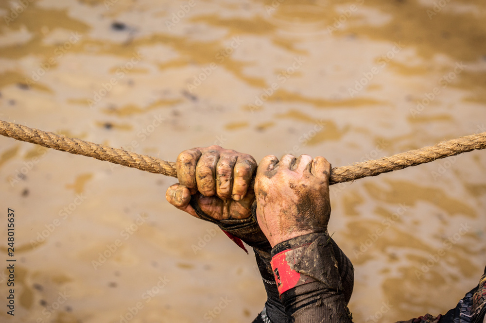 Mud race runners, defeating obstacles by using ropes. Details of the ...
