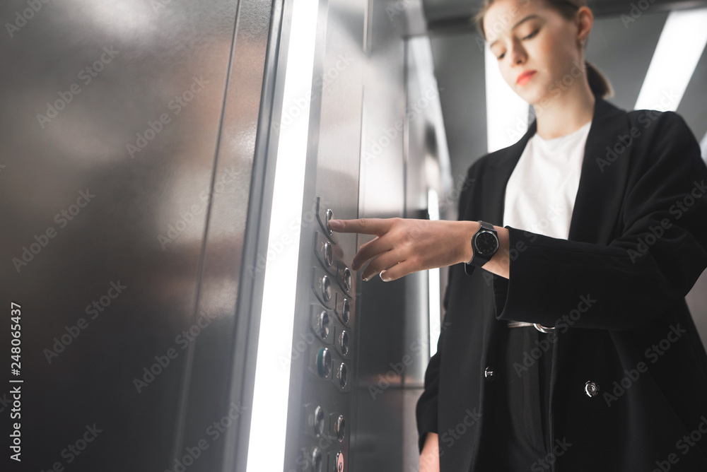 Diligent businesswoman pressing button inside elevator with a watch on ...