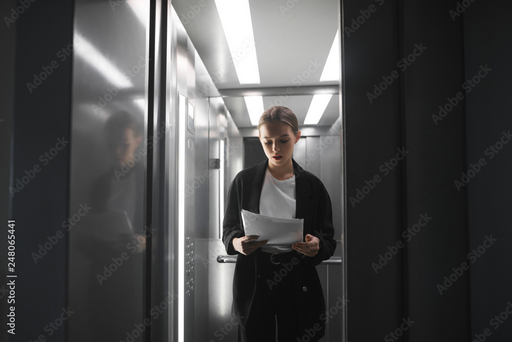 Foto de Busy concentrated office worker is reading the documents while the elevator door is ...
