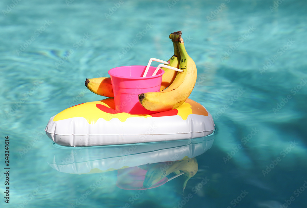 Two bananas with painted faces are drinking from a pink glass of juice ...