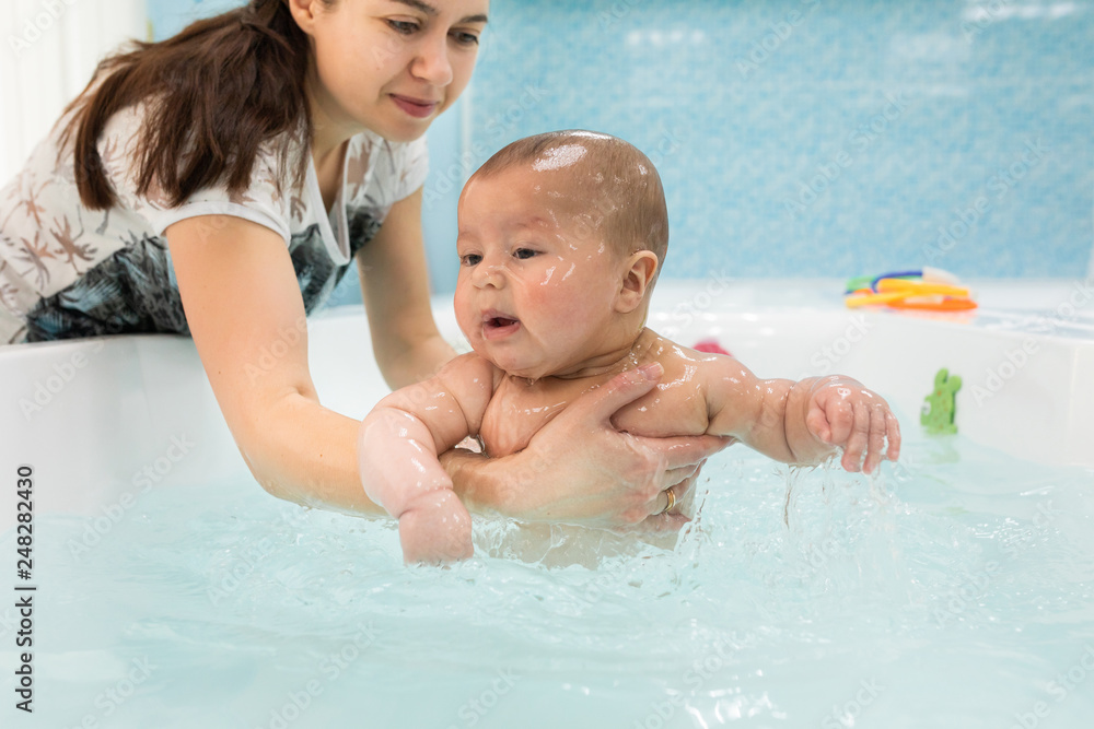 Newborn baby swimming in the bath or bathtub. Mother help him swim. Mom ...