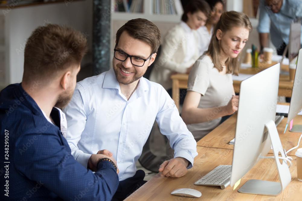Friendly happy employee handshaking colleague at workplace thanking for ...