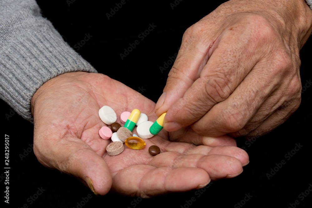 An elderly man holds a lot of colored pills in old hands. Painful old ...