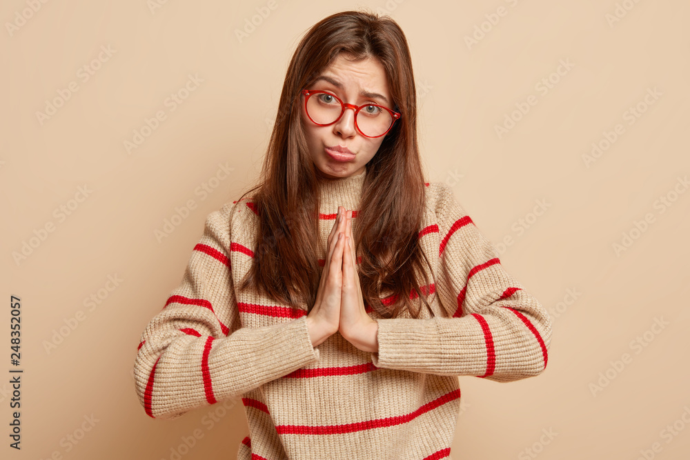 Regretful brunette woman keeps palms pressed together, feels guilty ...