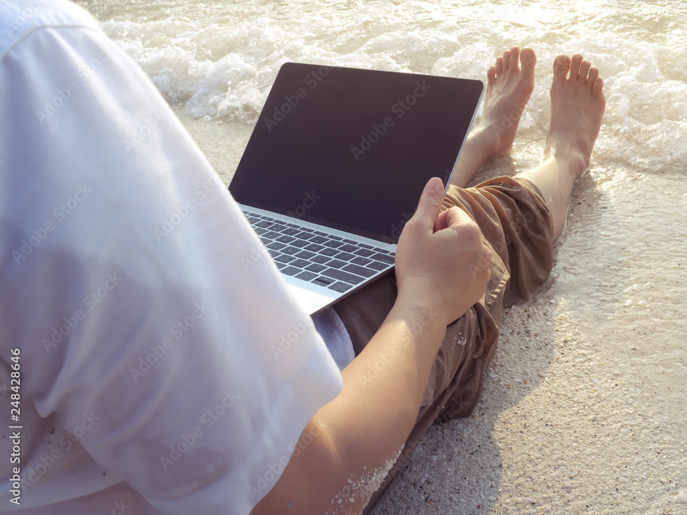Relaxed young man with laptop sitting on the sandy beach with soft ...