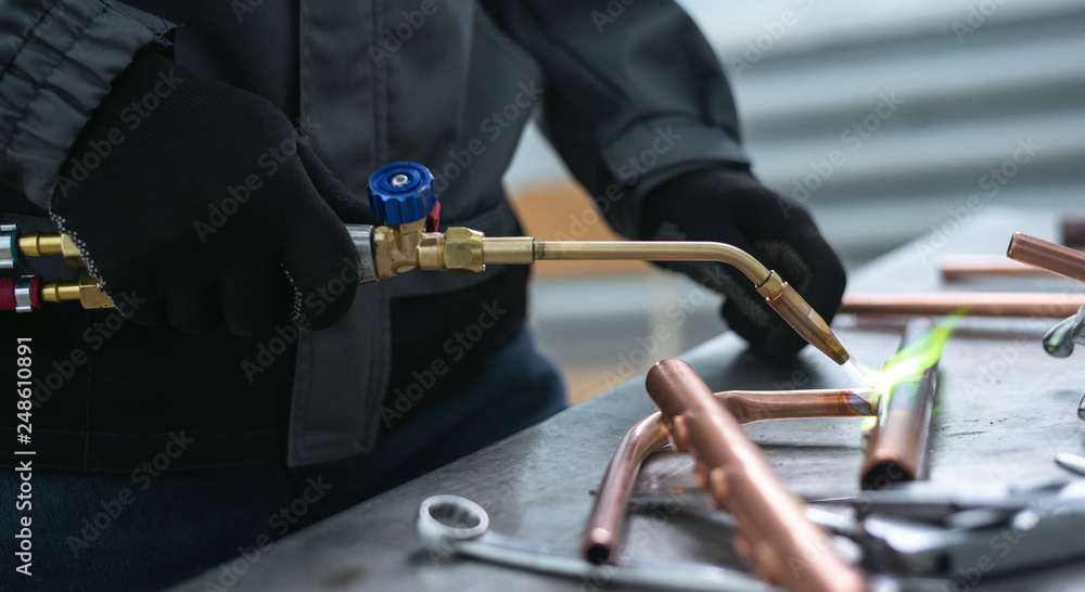 Worker is soldering a pipe by a blow lamp on a factory workbench ...