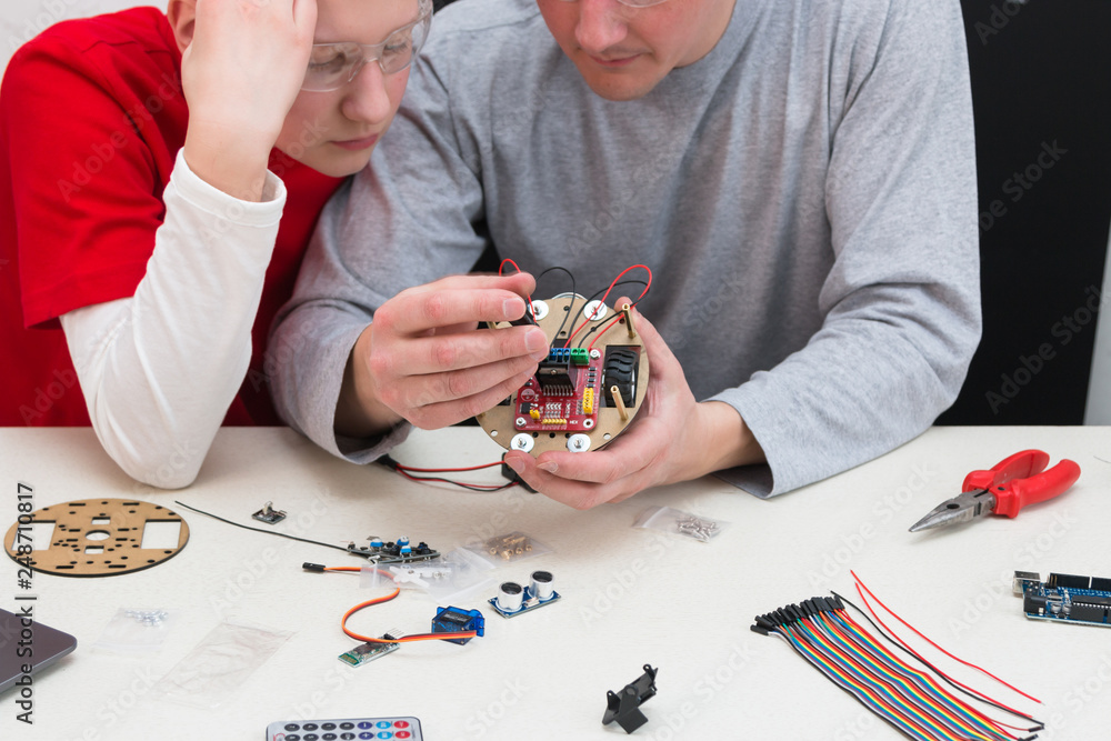 A teenager boy with his dad teacher collects a handmade robot working ...
