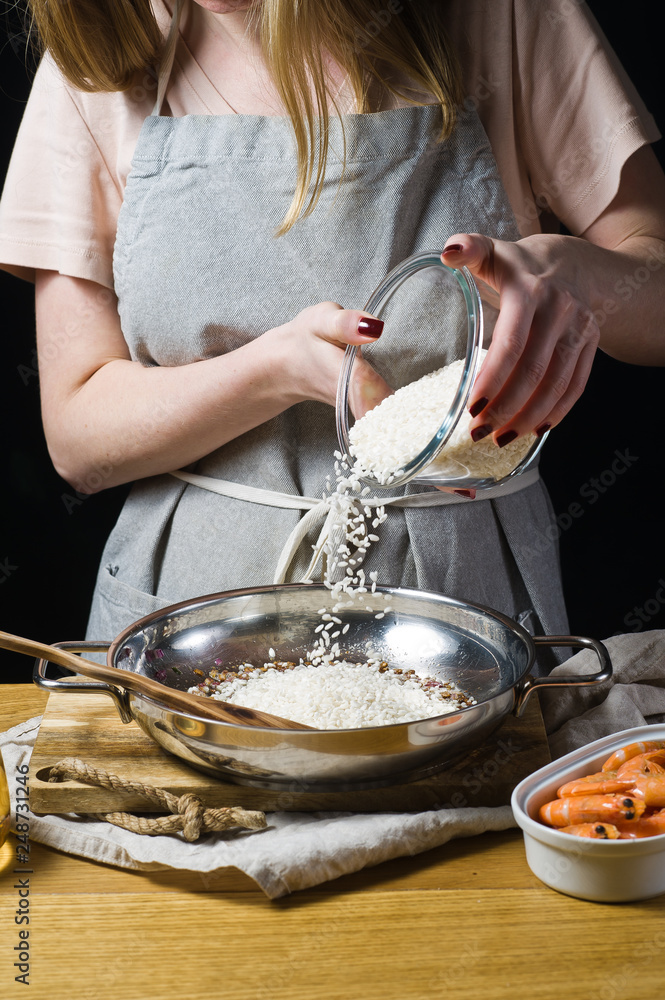 The chef puts the rice in the pan for Italian risotto. Shrimp, white ...