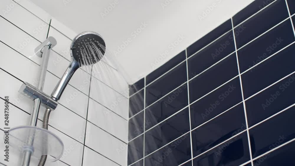 A static shot of a chrome shower head coming on, the water blasts out ...