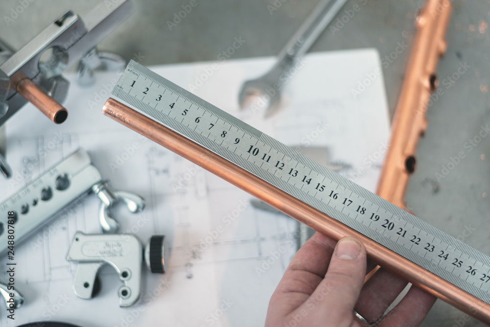 Worker is measuring a pipe by a straightedge on a fitter workbench ...