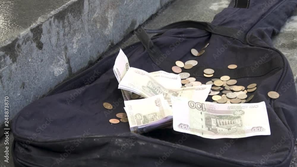 Money falling on black guitar case on outdoor city sidewalk. Close up ...