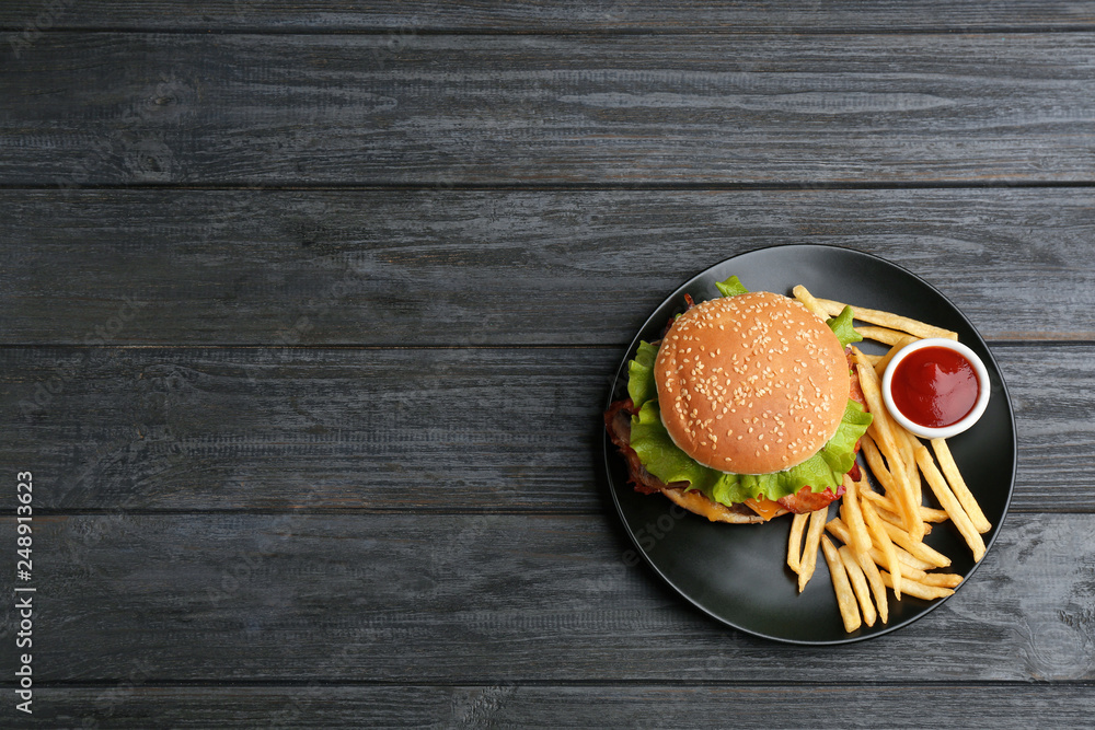 Plate with tasty burger, french fries and sauce on wooden background ...