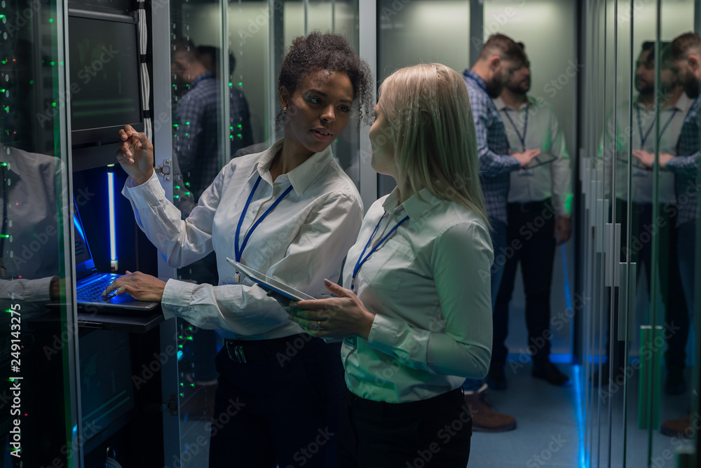 Two women are working in a data center with rows of server racks Stock ...