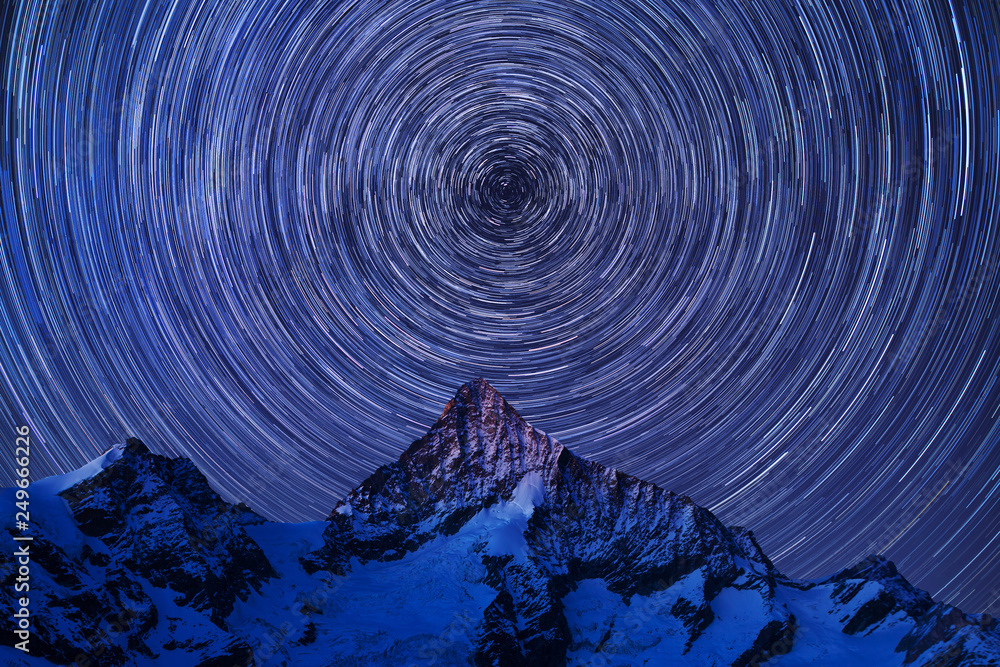 Incredible night view in Swiss Alps. Star trails moving in blue sky ...