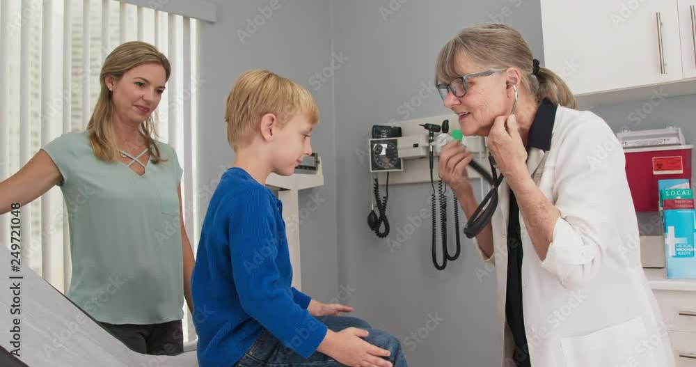 Female pediatrician using stethoscope on child patient with mother in ...