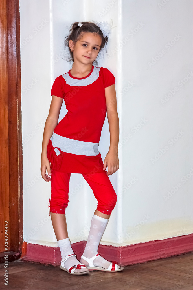 portrait of innocent little girl standing against a gray wall, she is ...