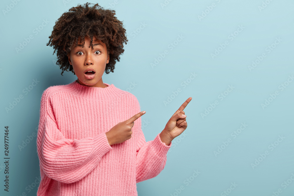 Scared black lady with curly hair, wears casual jumper, points at upper ...