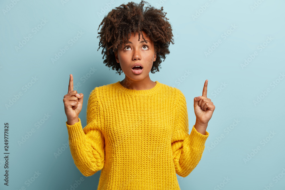 Fascinated dark skinned lady with curly hair, dressed in yellow sweater ...