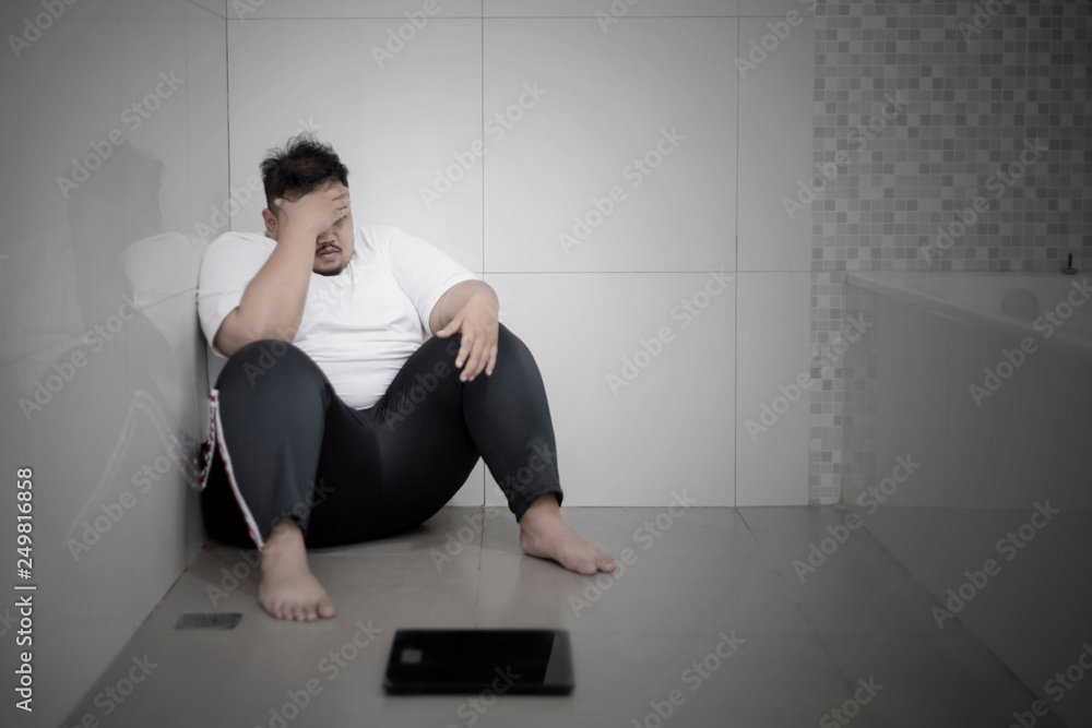 Depressed fat man sitting with a scale Stock Photo | Adobe Stock