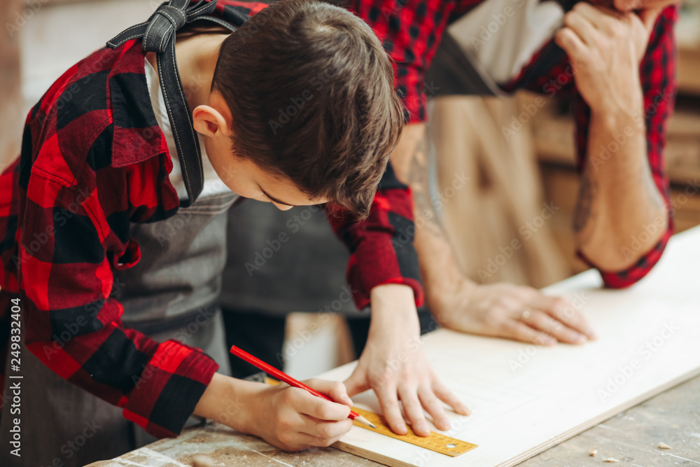 Hardworking little boy is busy taking measure and marking of wooden ...