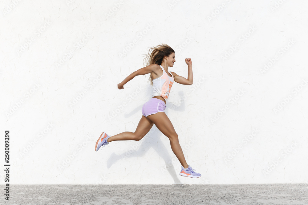 Strong athletic happy sportswoman wearing sport shorts jump across ...