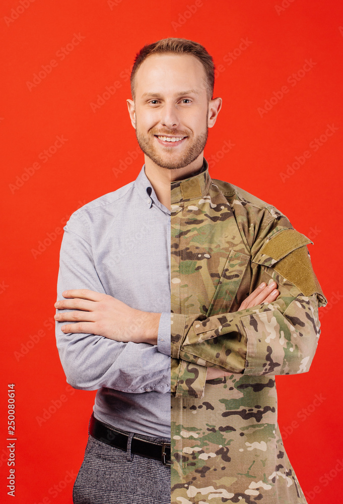 Young soldier in military wear keeping arms crossed and smiling on red ...