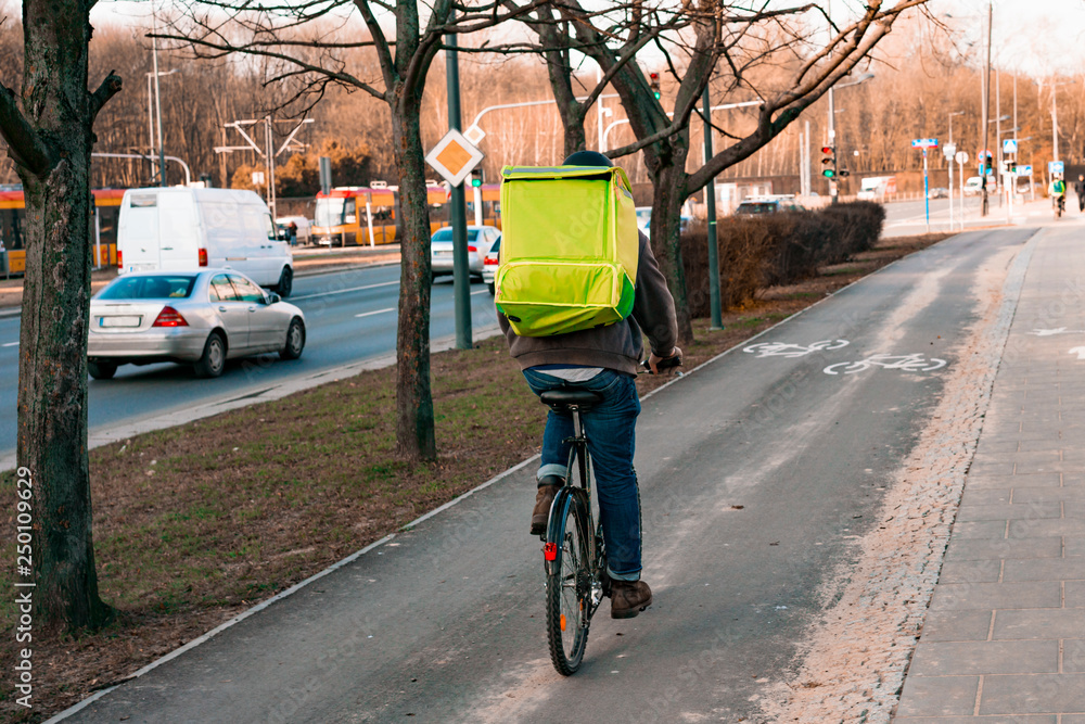 Food delivery driver with green backpack on a bicycle riding along a ...
