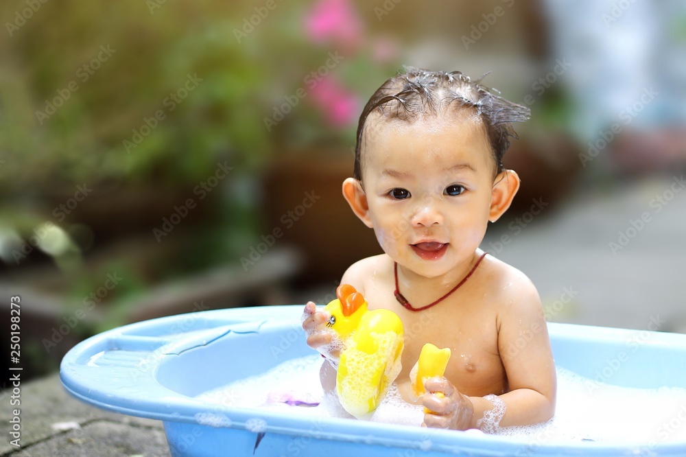 A happy baby child take a shower with a duck toys. She sitting in a ...
