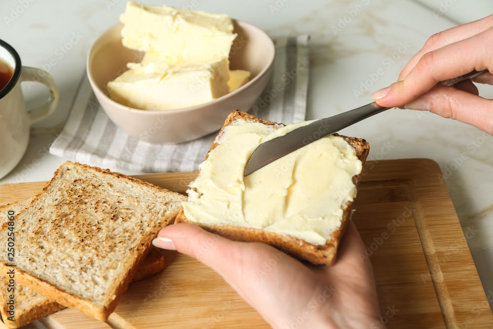 Woman spreading tasty toast with butter at table Stock Photo | Adobe Stock