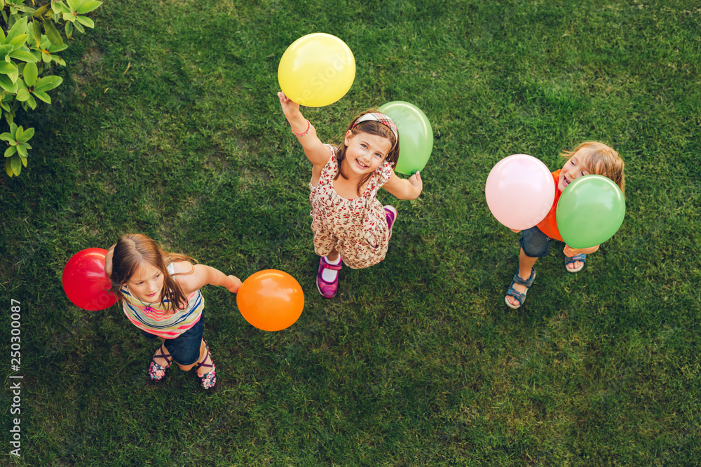 Three happy little kids playing with colorful balloons outdoors, top ...