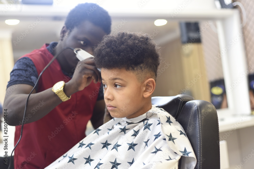 Boy in the african barbershop. Cute mixed boy makes a haircut in the ...