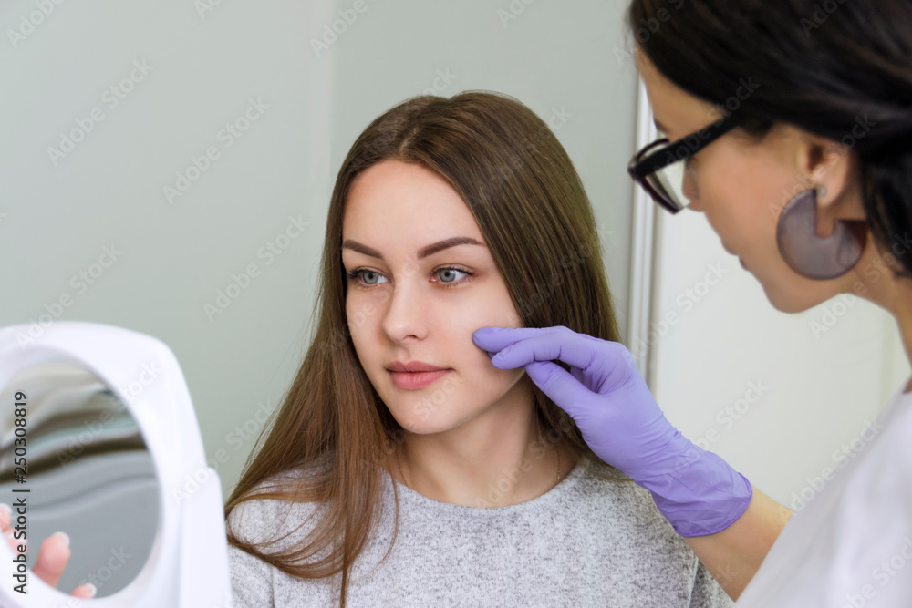 Female cosmetologist showing to young pretty woman the face zones to ...
