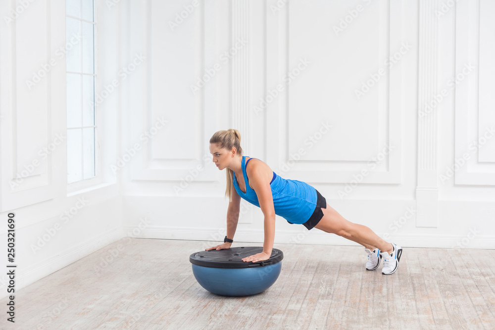 Focused sporty beautiful young athletic blonde woman in black shorts and blue top working in gym ...