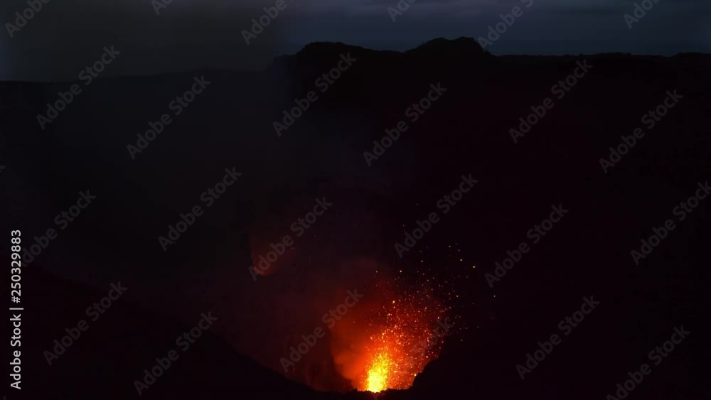 Orange lava and ashes are blown up high in the air during a roaring ...