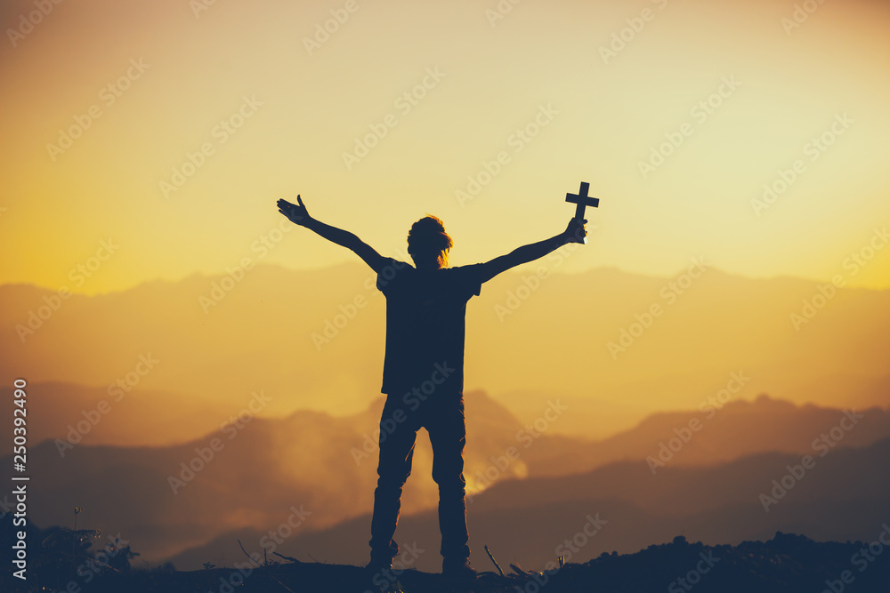 Man standing holding christian cross for worshipping God at sunset ...