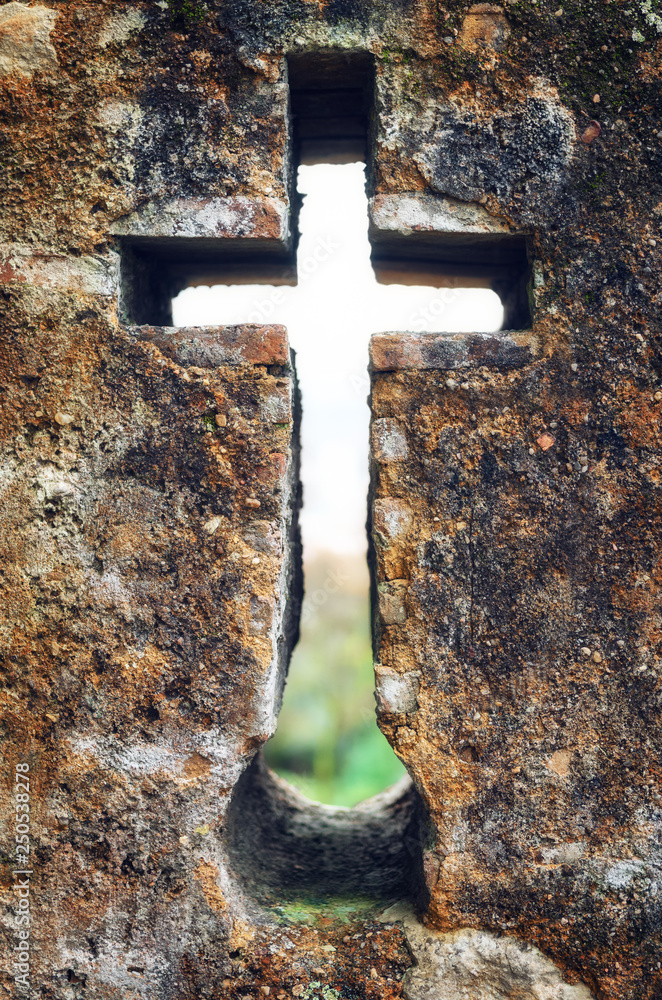 ancient medieval cross shaped arrow slit on the wall of an old castle ...
