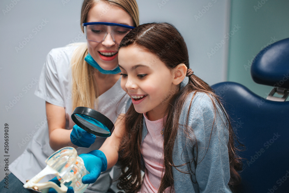 Amazed girl sit in dental chair in room. She look at artificial jaw ...