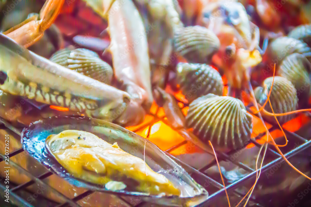 Close up grilled crabs and clams on fire charcoal stove at night party ...