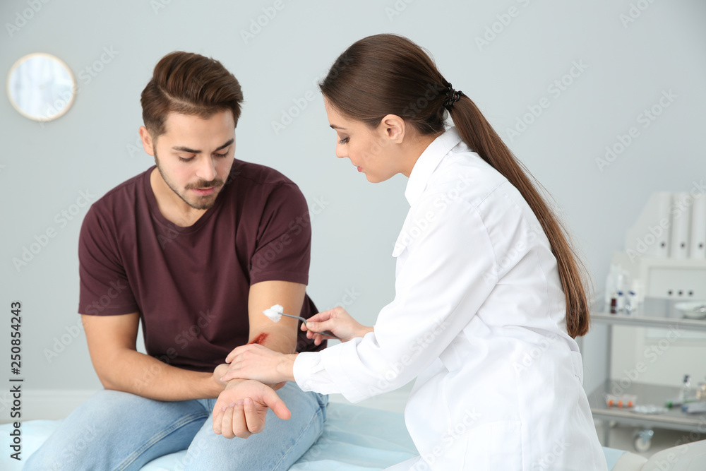 Female doctor cleaning young man's arm injury in clinic. First aid ...