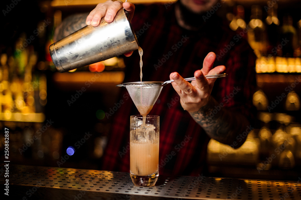 Bartender pouring a Singapore Sling cocktail from the steel shaker through the strainer Stock ...