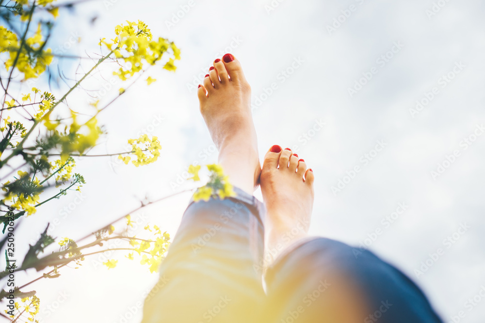 Legs up of happy female lying in deep yellow flowers meadow with bright ...