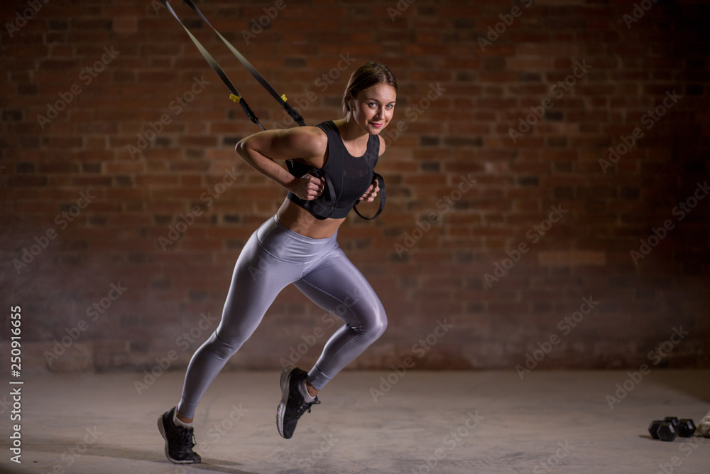 Fitness woman trainin on the TRX in the gym, doing Sprinter Start exercise where stabilizing ...