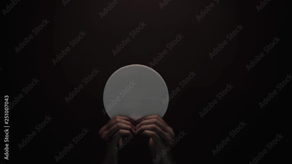 Vidéo Stock Priest hands raising a communion bread on dark background ...