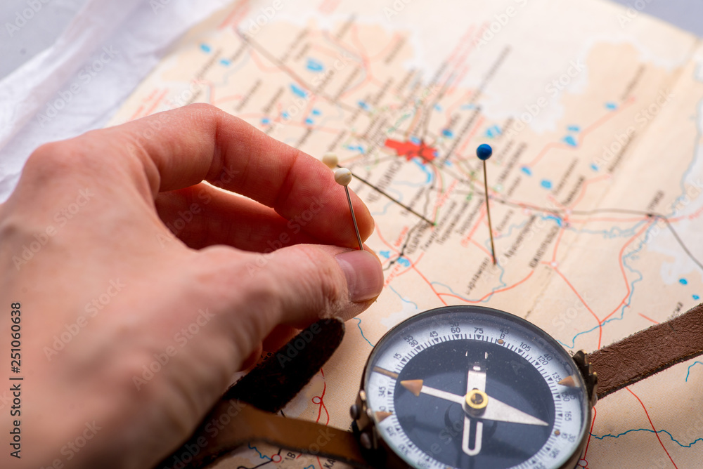 hand marks places on the map with pins. Сompass on a leather belt on ...
